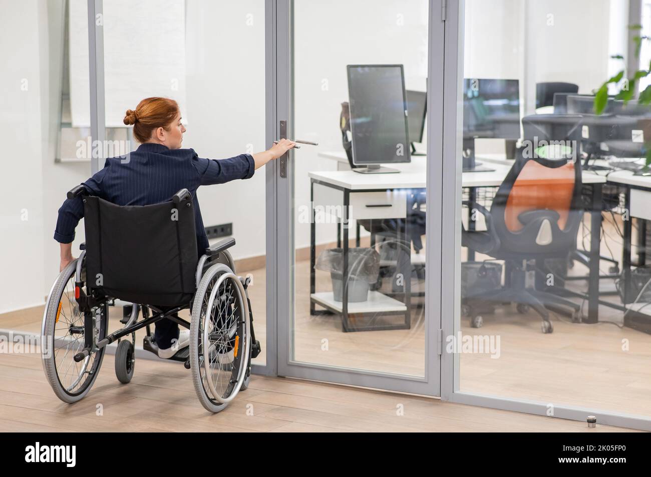 Red-haired caucasian woman in a wheelchair trying to open the door in ...