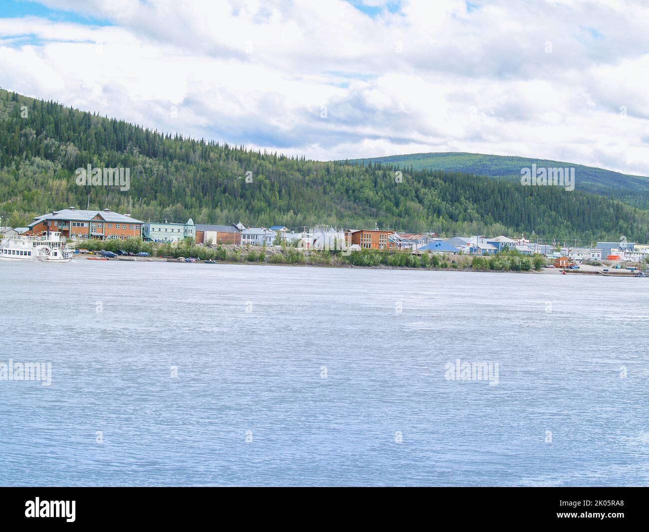 Dawson City across the Yukon River with rolling tree clad hill ...