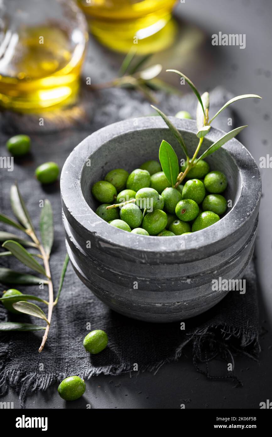 Green and small raw olives with mortar and a twig. Freshly picked green ...