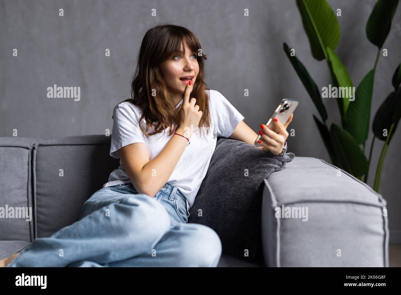 Happy young woman using phone while sitting a couch at home with laptop ...