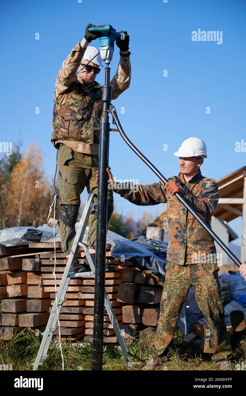 Male workers building pile foundation for wooden frame house. Men ...