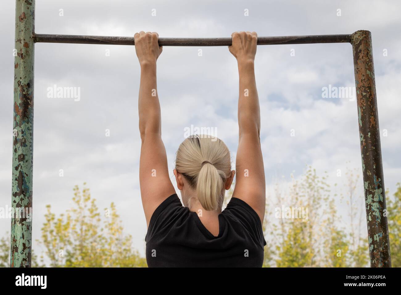 girl hanging on the crossbar on the sports ground. gymnast hanging on ...