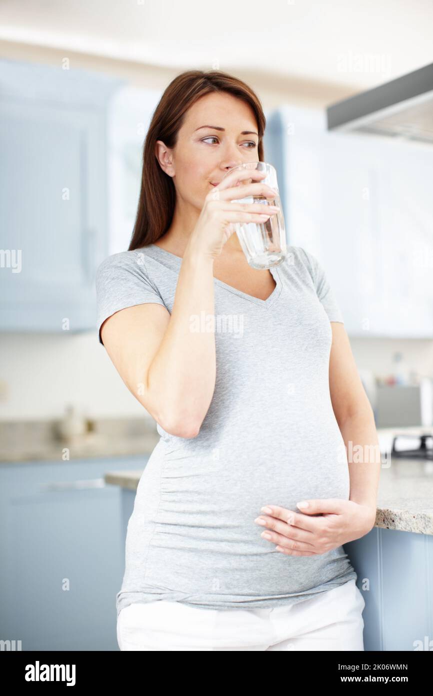 Conscientious about the health of her baby. A smiling pregnant woman drinking water in the ...