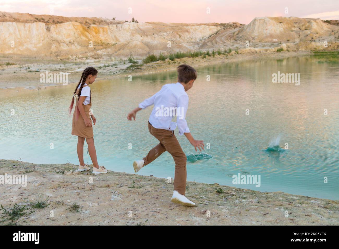 Teenagers 8-9 years old throw stones into water from shore, outdoor ...