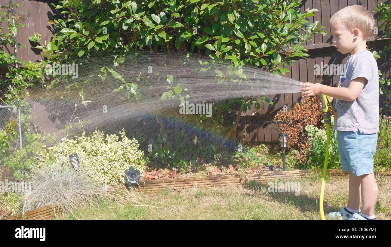 Funny little boy watering lawn plants in garden housing backyard ...
