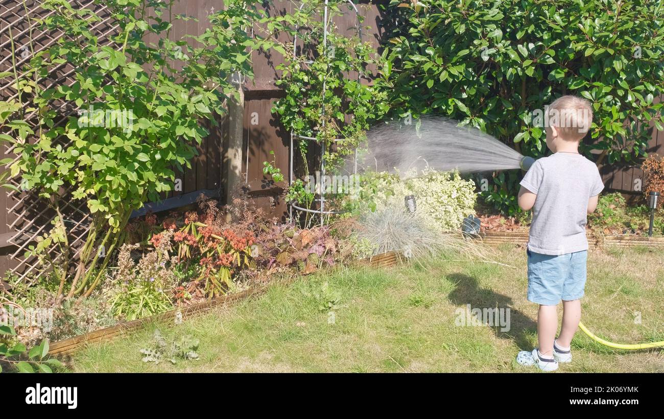 Funny little boy watering lawn plants in garden housing backyard ...