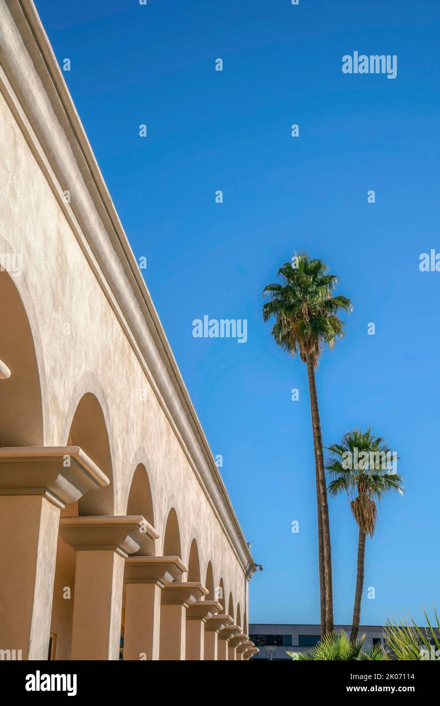 Facade of a building with arches and columns against blue sky and palm ...