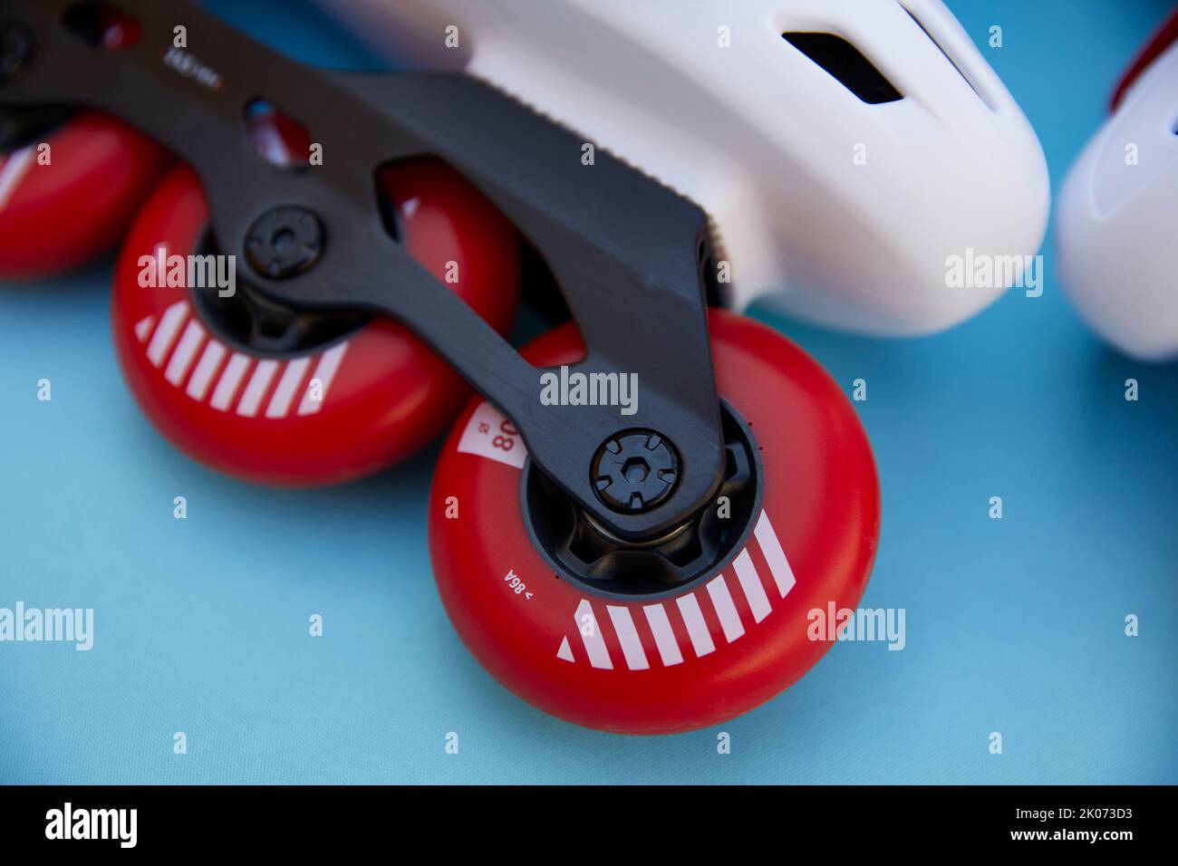 Close-up of the front wheel of white inline skates on a blue background ...