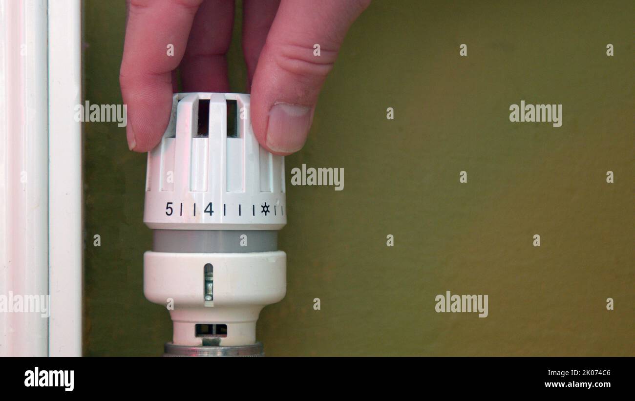 Hand turning down radiator heating to save money Stock Photo - Alamy