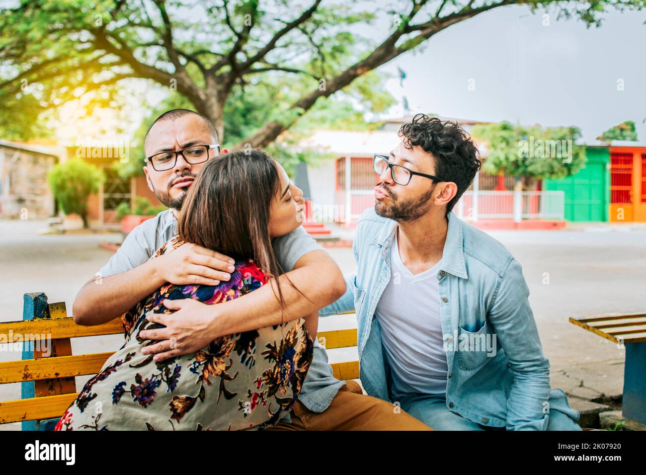 Unfaithful girlfriend hugging her boyfriend in a park secretly kissing another man. Couple ...