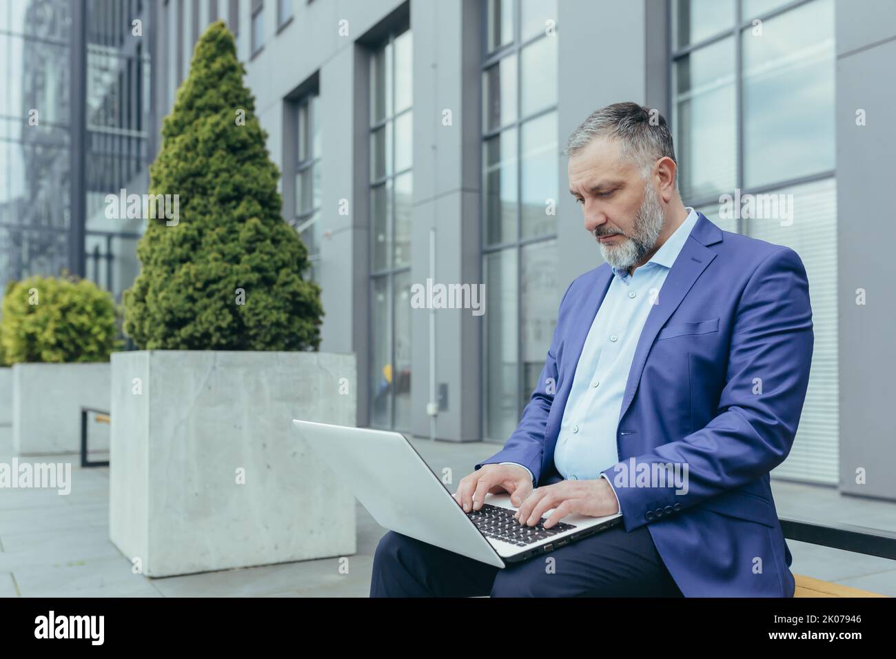 Senior handsome male businessman in suit working with laptop online ...