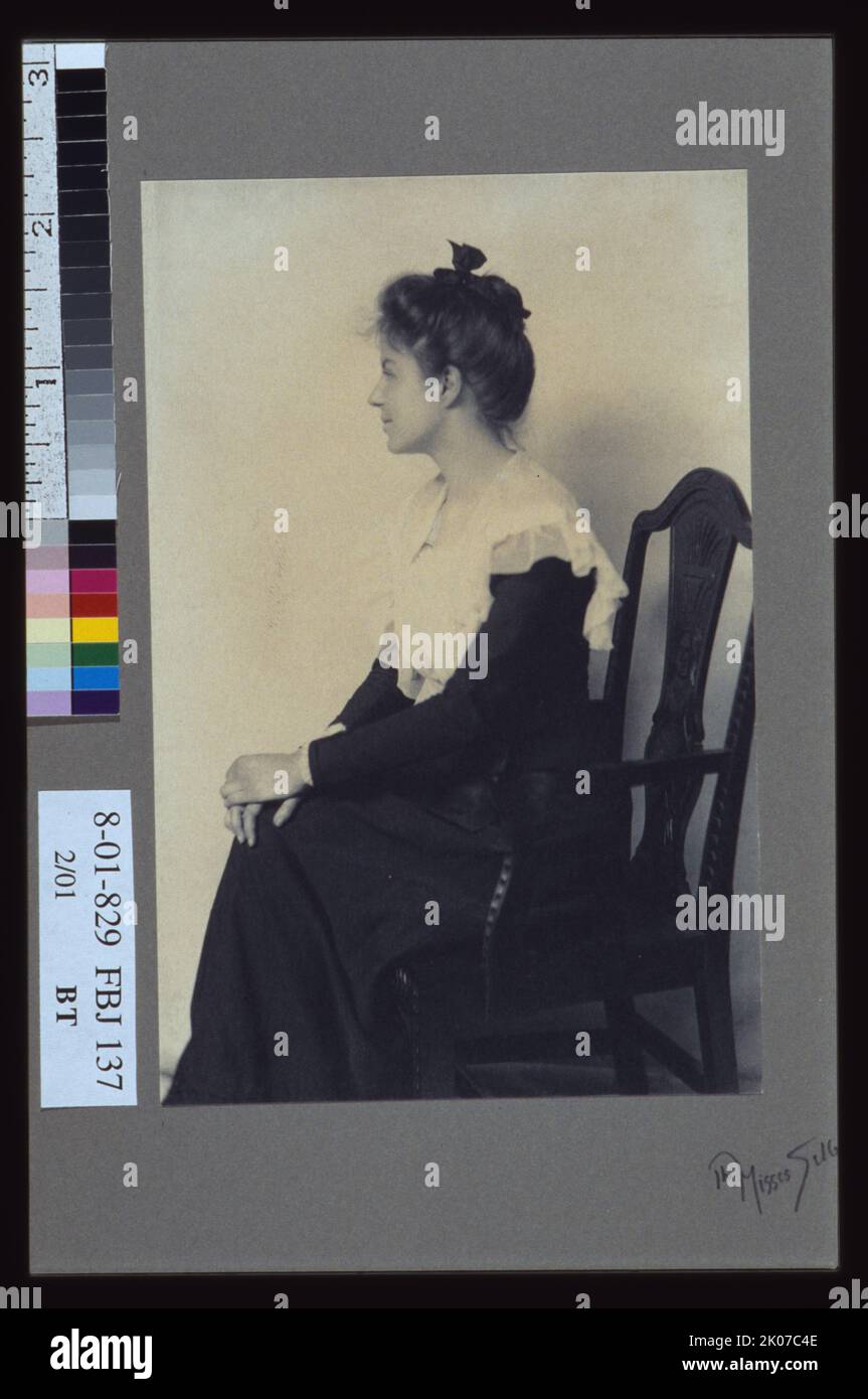 Profile portrait of a woman seated in chair, facing left with hands on ...