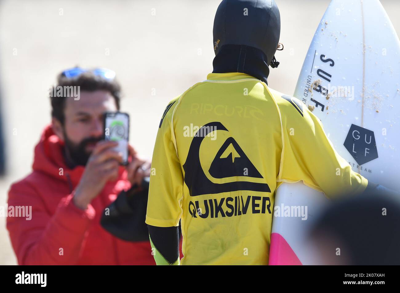 Surfer in yellow quicksilver rash vest being photographed on mobile ...