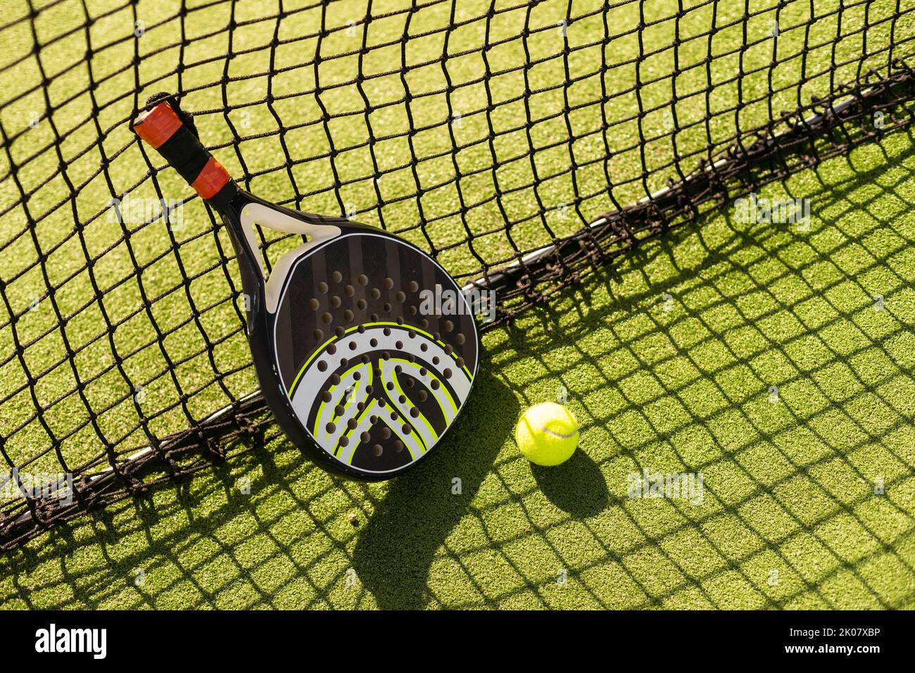 Yellow balls on grass turf near padel tennis racket behind net in green ...