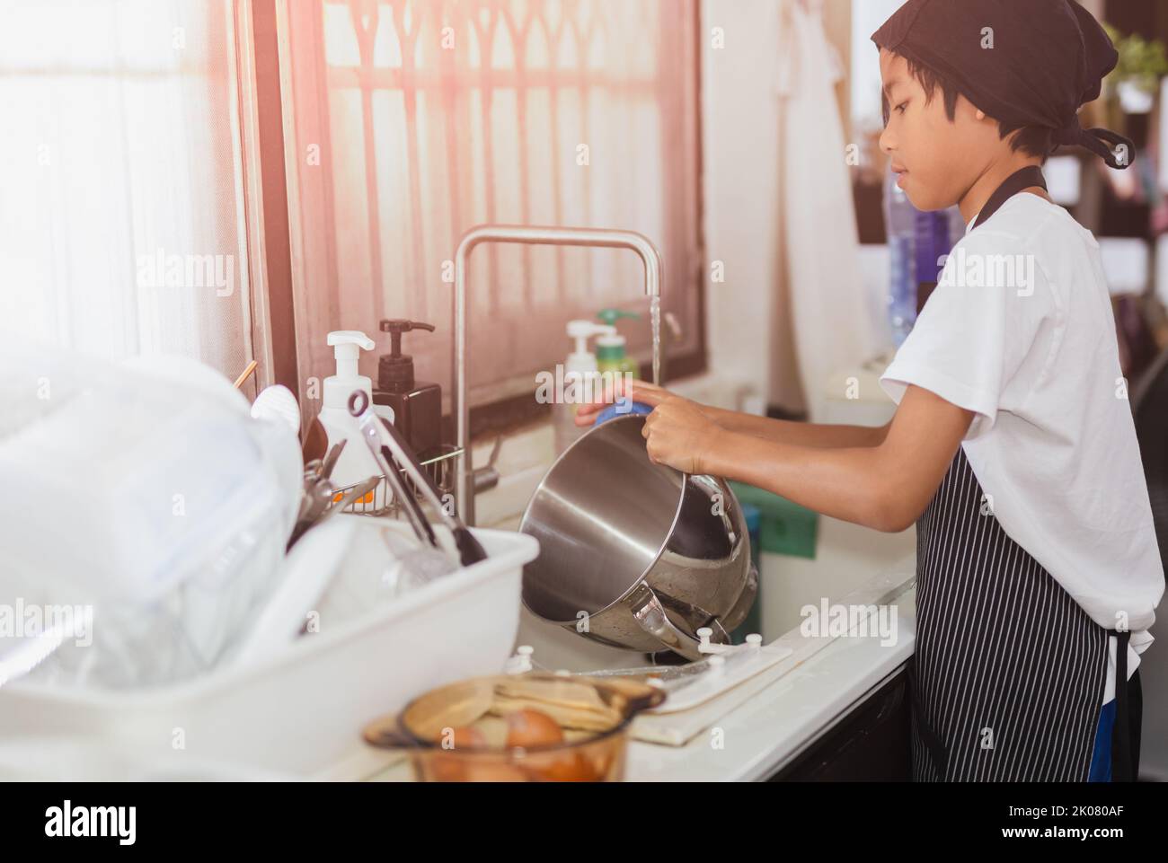 Young boy with apron doing the dishes at kitchen sink in the house ...