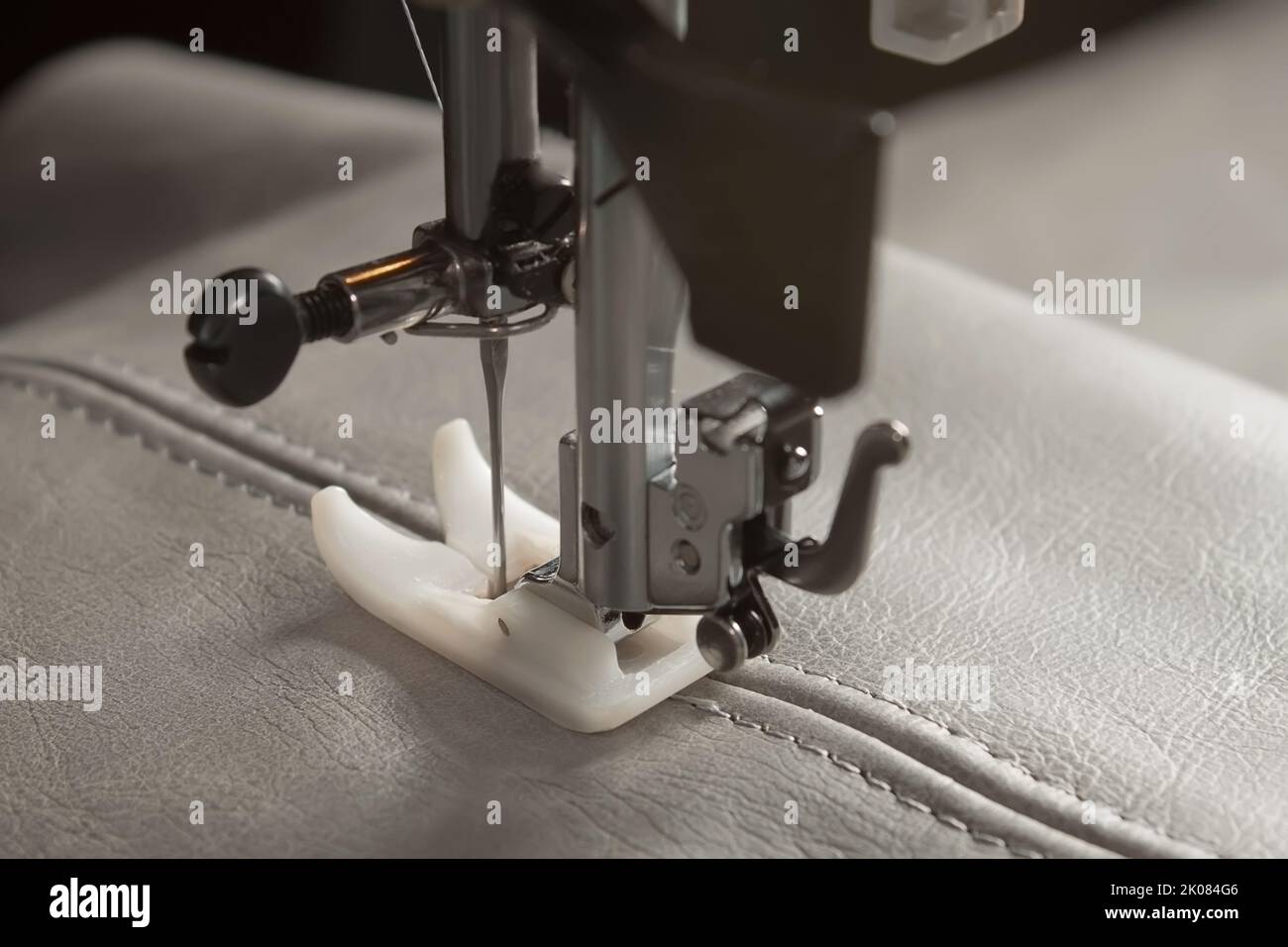 Modern sewing machine with special presser foot makes a seam on grey ...