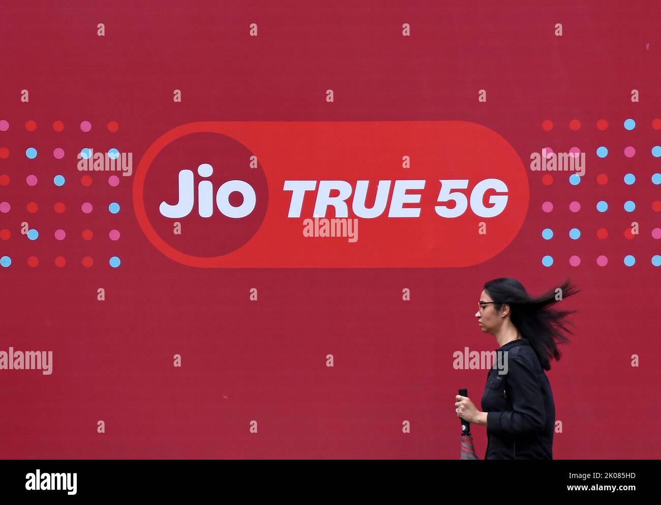 A woman holding an umbrella walks past Jio 5G branding in Mumbai. Reliance Jio 5G network ...