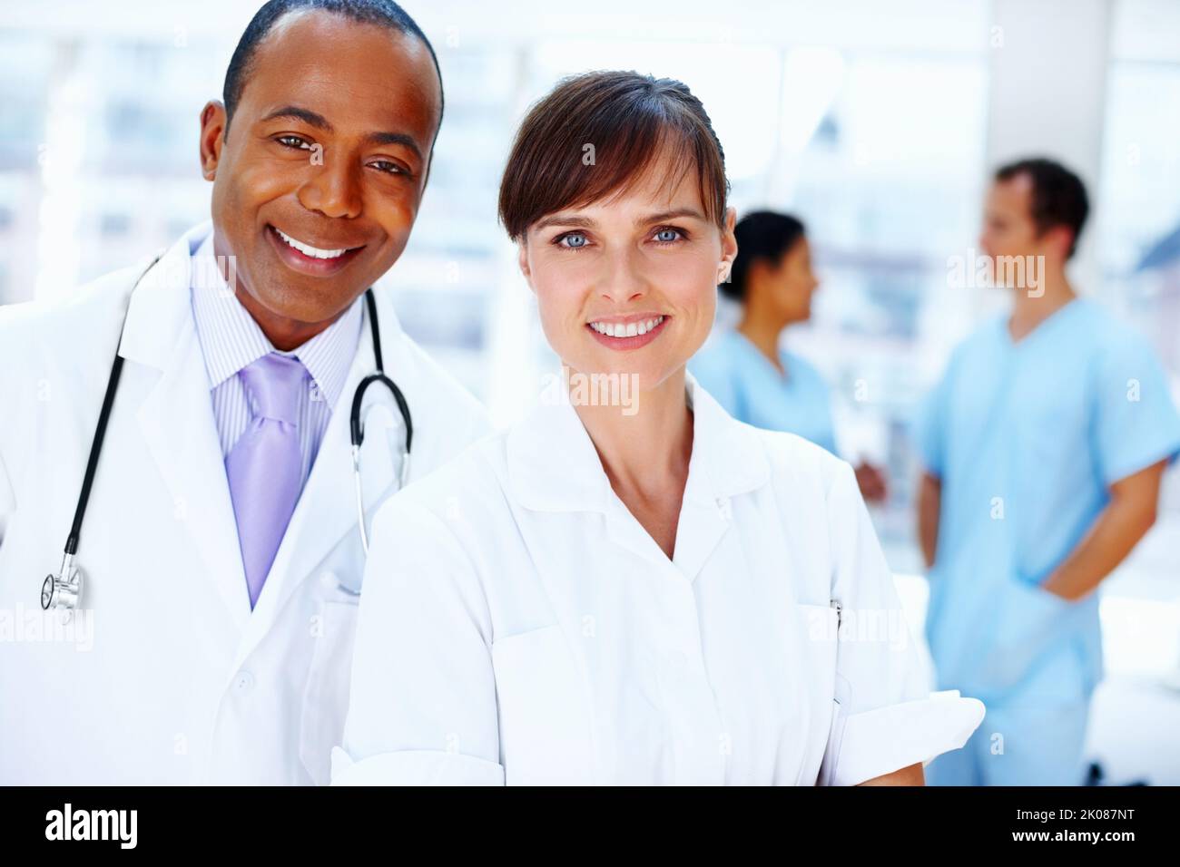 How can we help. Closeup of happy doctors with nurses in background ...