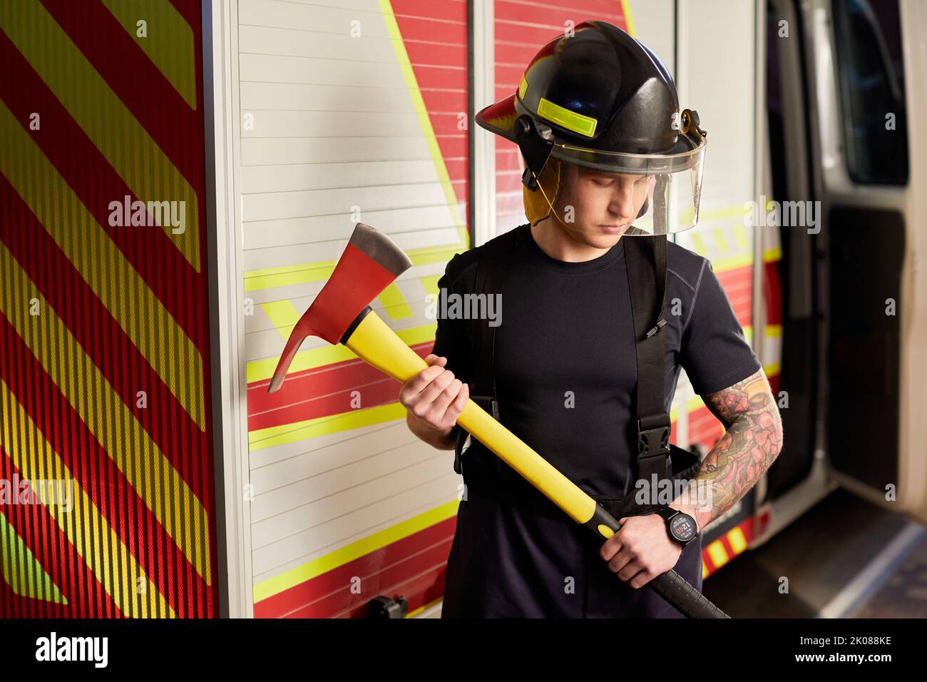 Photo of fireman wearing helmet with ax against fire engine Stock Photo ...