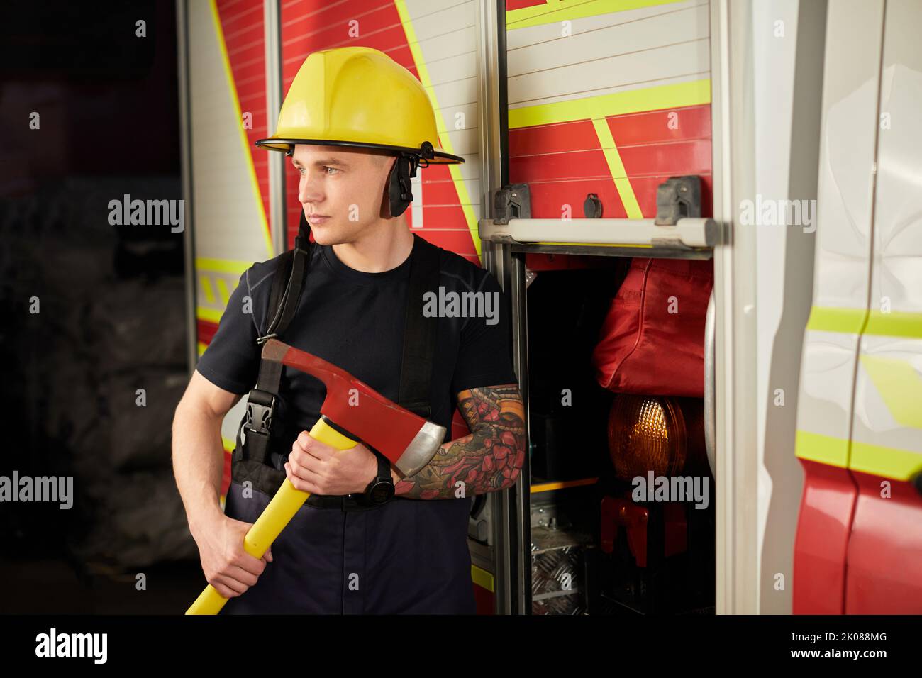 Photo of fireman wearing helmet with ax against fire engine Stock Photo ...