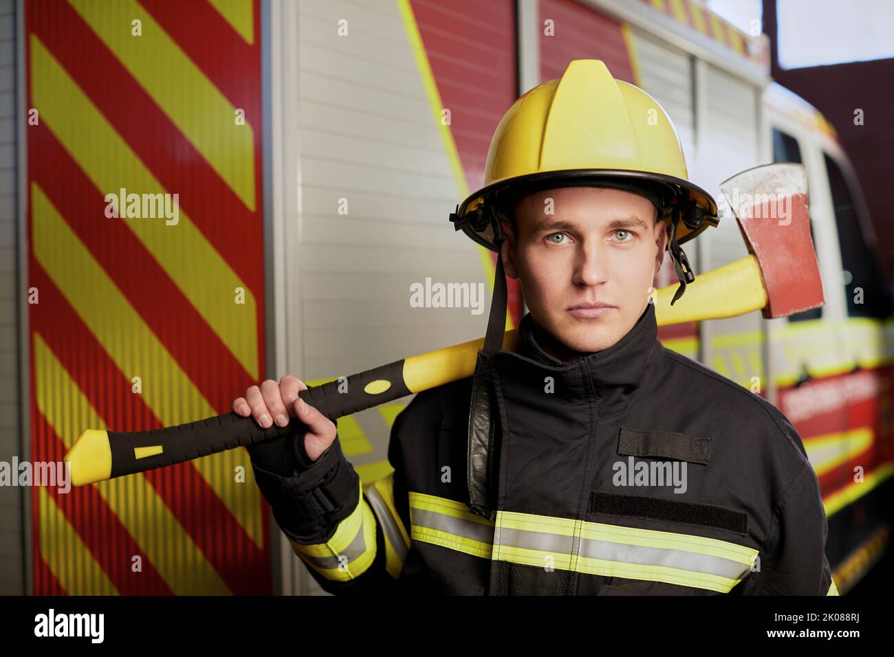 Firefighter fully equipped with helmet and ax in fire truck background ...