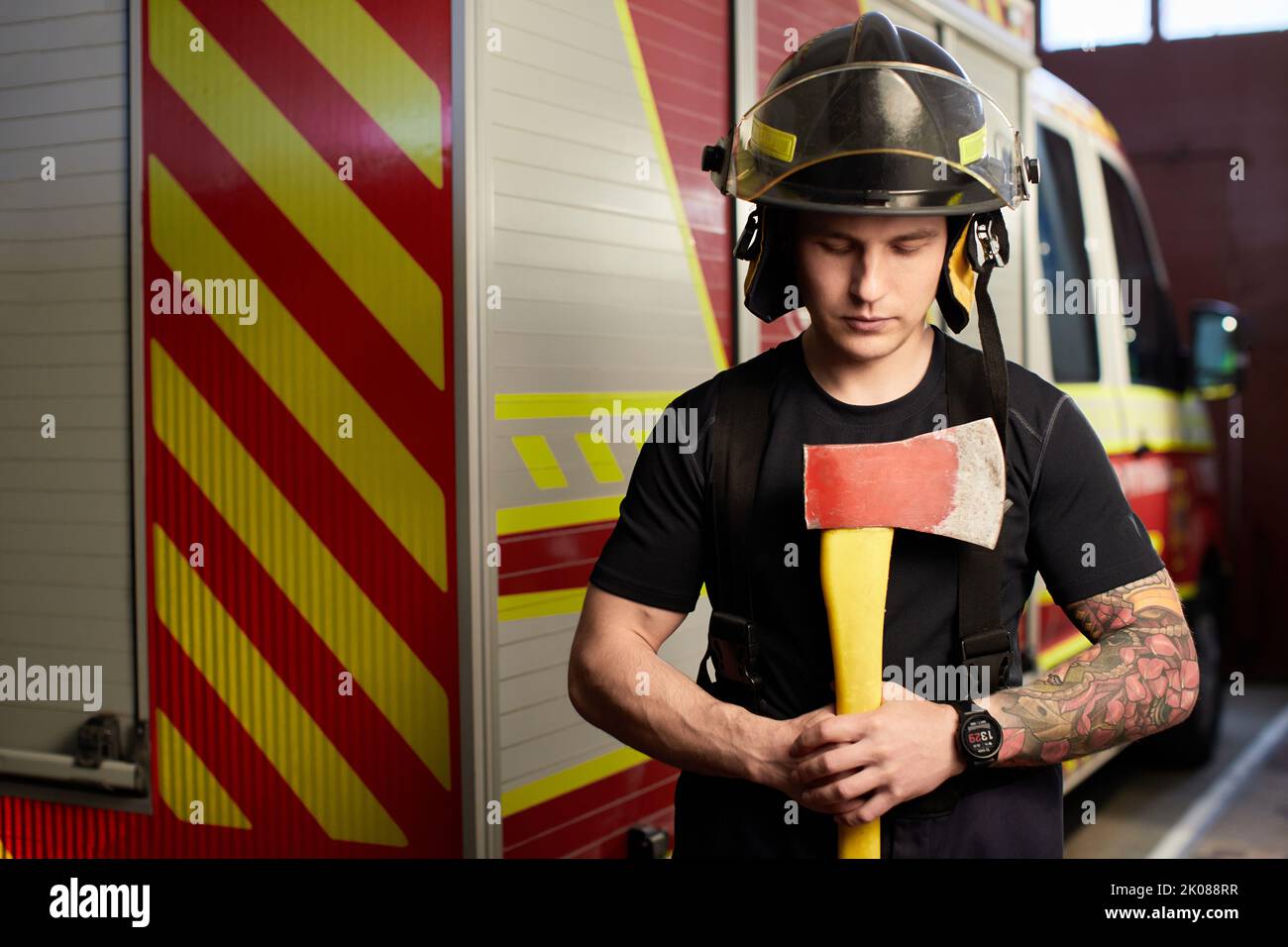 Photo of fireman wearing helmet with ax against fire engine Stock Photo ...