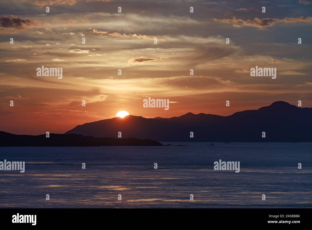 Sun sets behind distant blue mountains off coastal island Stock Photo ...