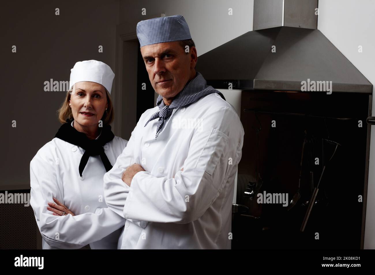 Two confident chefs with hands folded in commercial kitchen. Team of ...