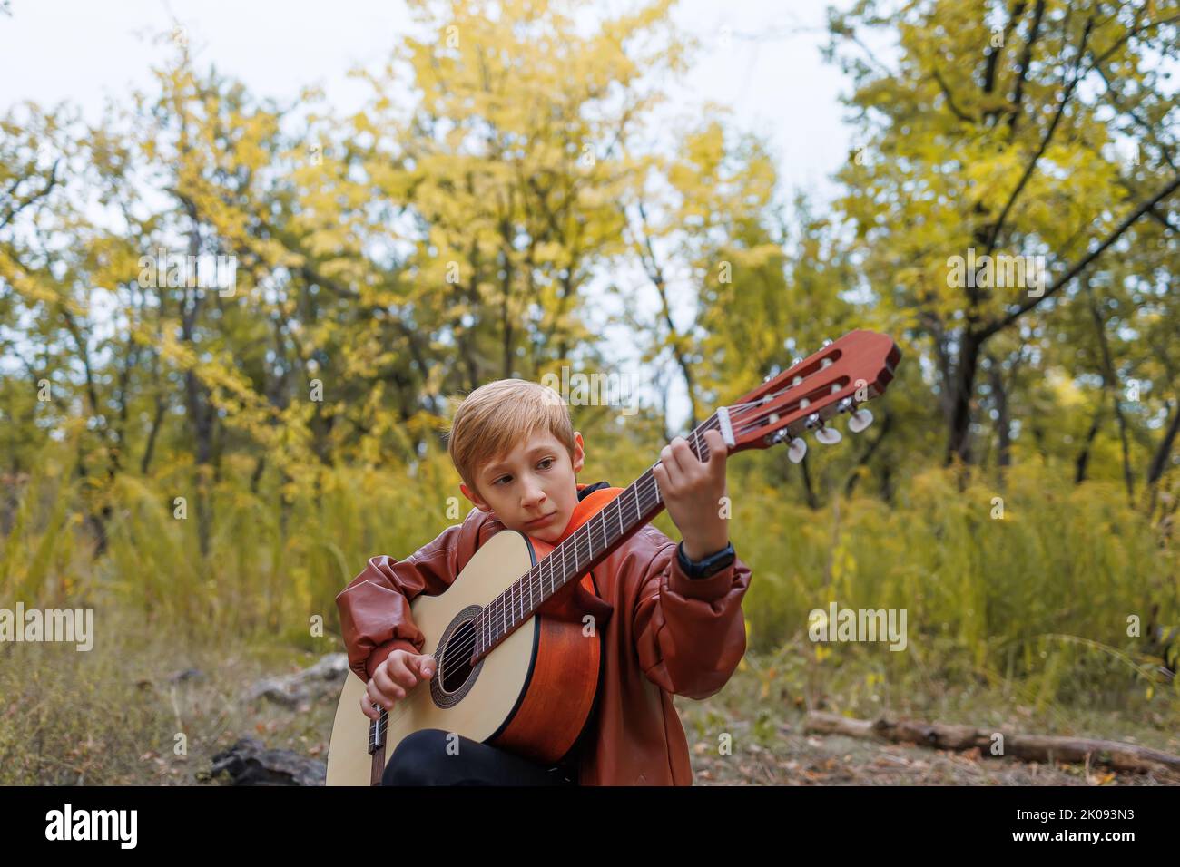 in autumn in the park a boy plays the guitar looks at the strings and ...