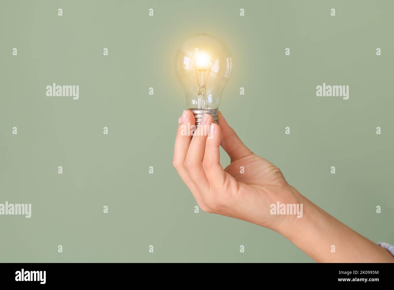 Female hand with glowing light bulb on green background Stock Photo - Alamy