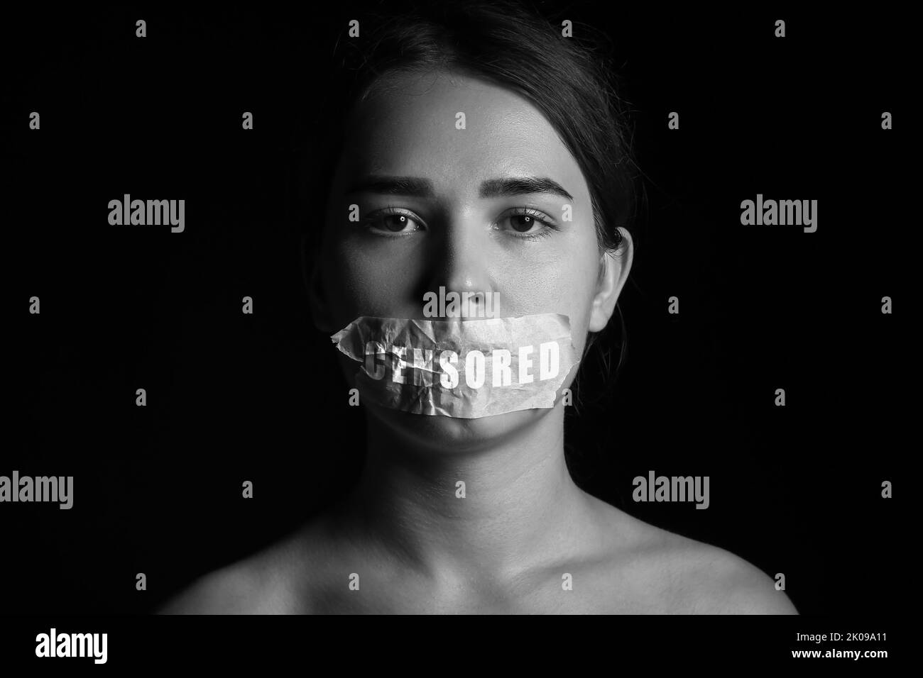 Black and white portrait of woman with taped mouth on dark background ...