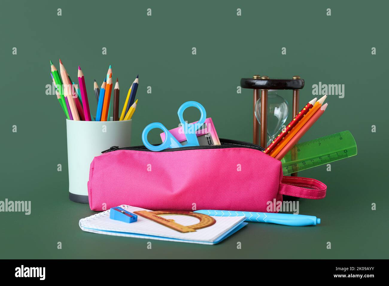 Pink pencil case with school stationery and hourglass on green ...