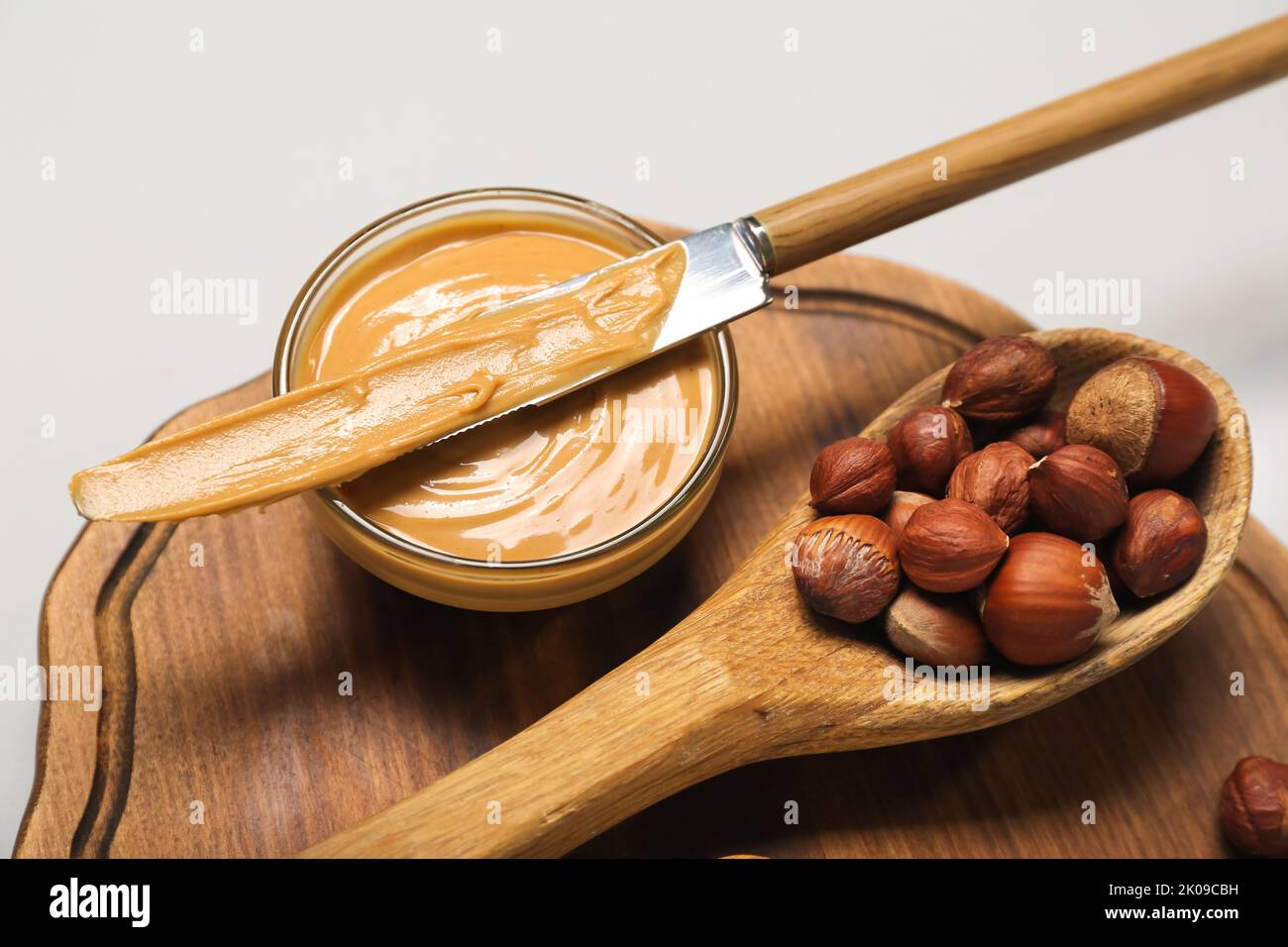 Wooden board with bowl of tasty nut butter and hazelnuts on white ...