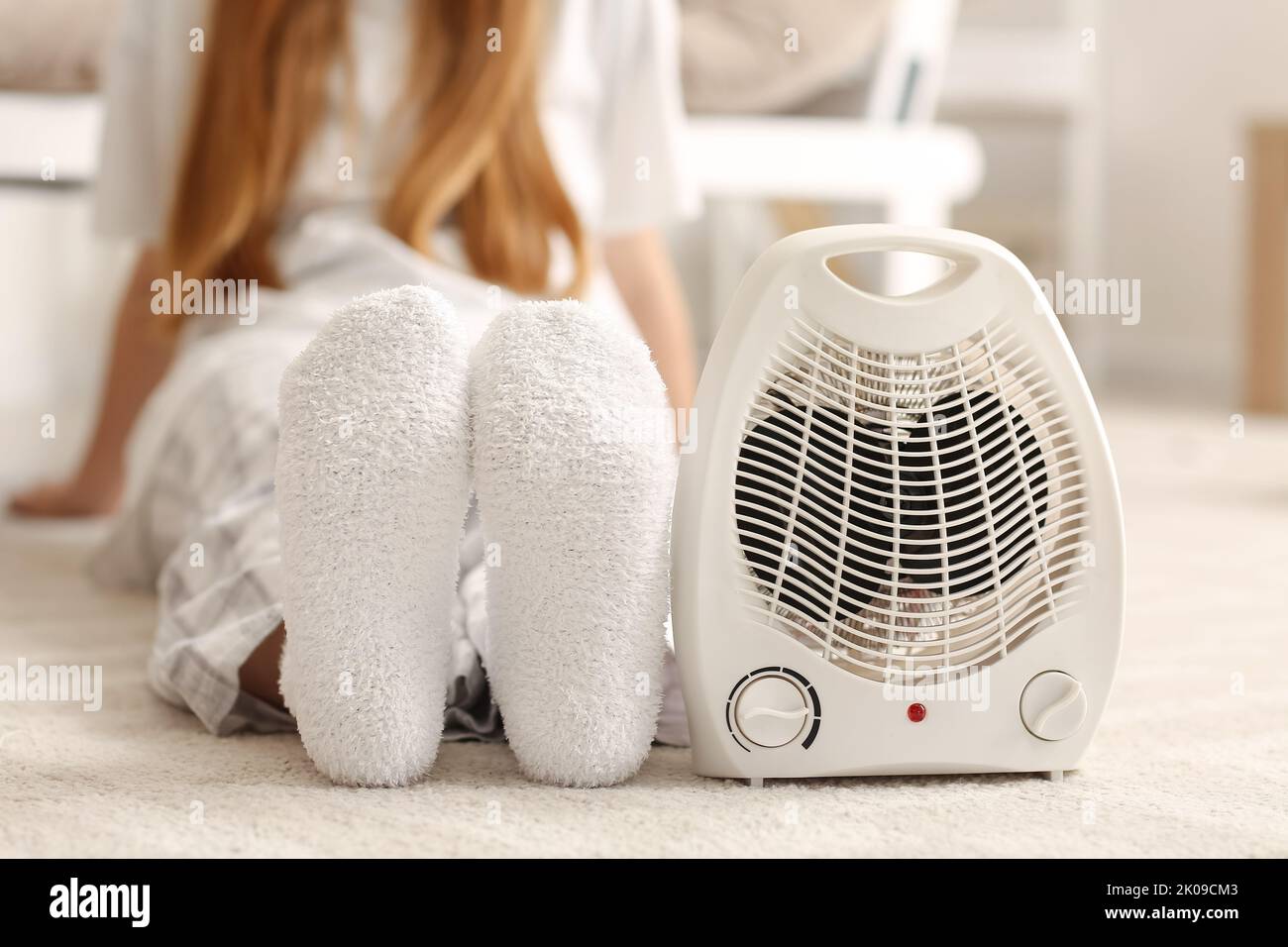 Electric fan heater and woman in warm socks on floor at home, closeup ...