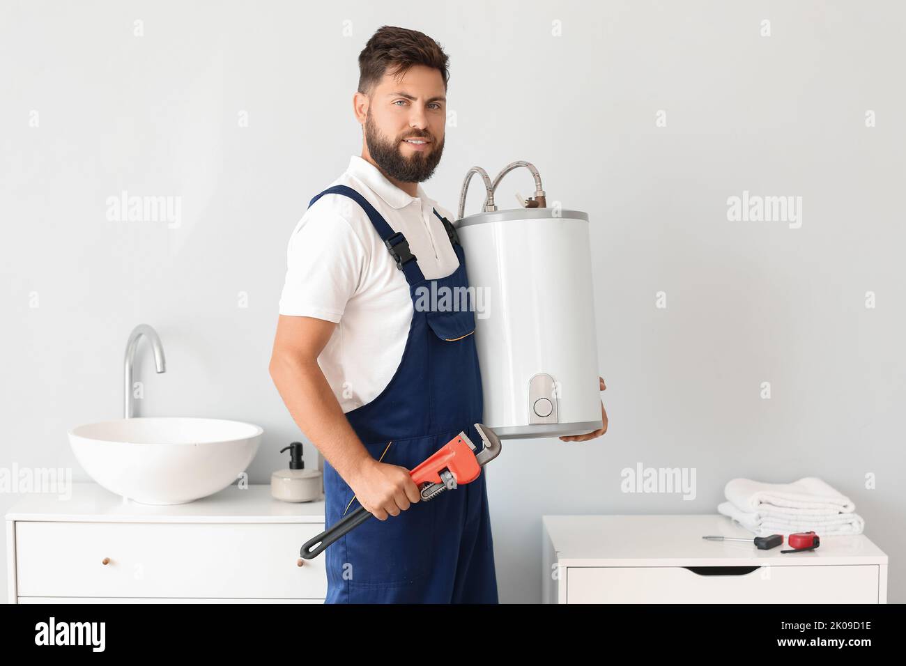 Male plumber with boiler and pipe wrench in bathroom Stock Photo - Alamy