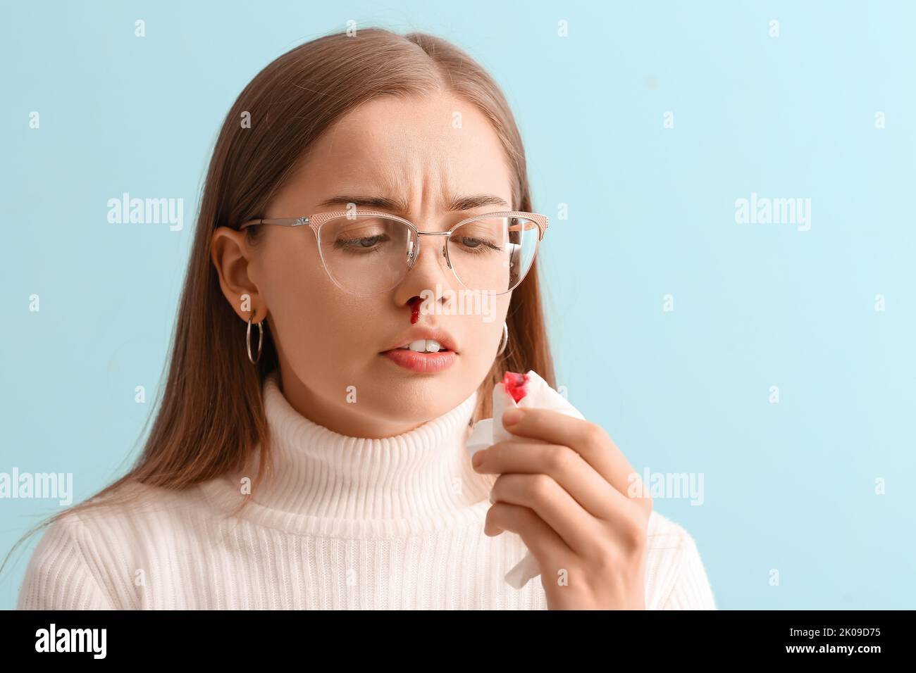 Young woman with nosebleed and tissue on blue background, closeup Stock ...