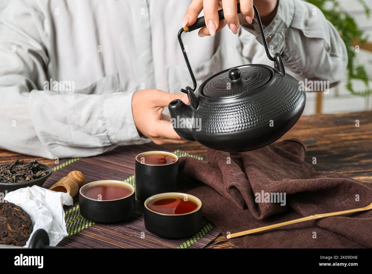 Woman pouring puer tea from pot at wooden table, closeup Stock Photo ...