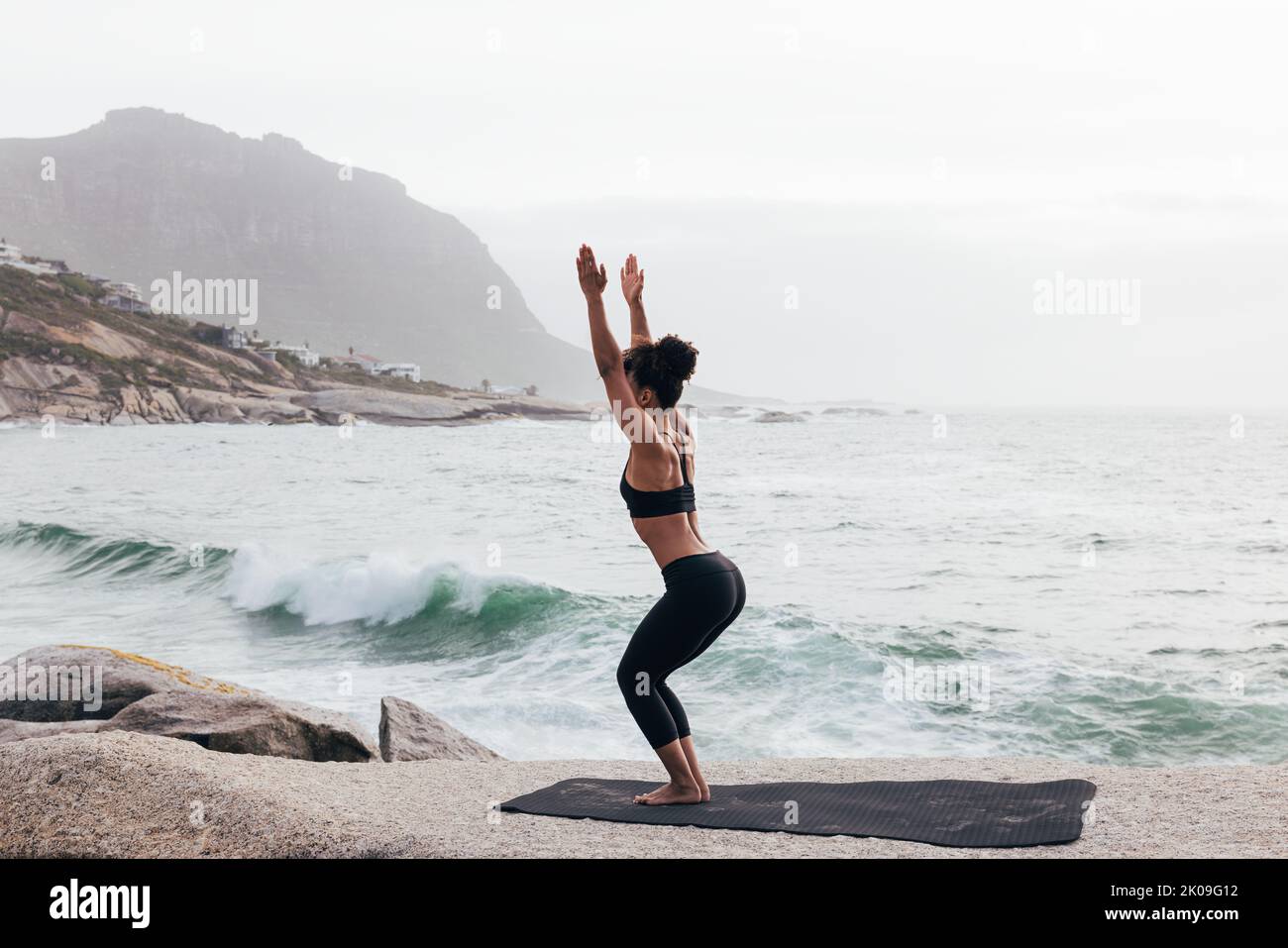 Young woman doing Utkatasana pose by ocean. Slim female in practicing ...