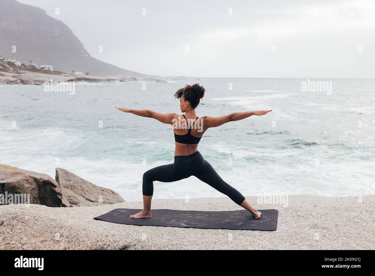 Rear view of slim female practicing warrior pose by ocean Stock Photo ...