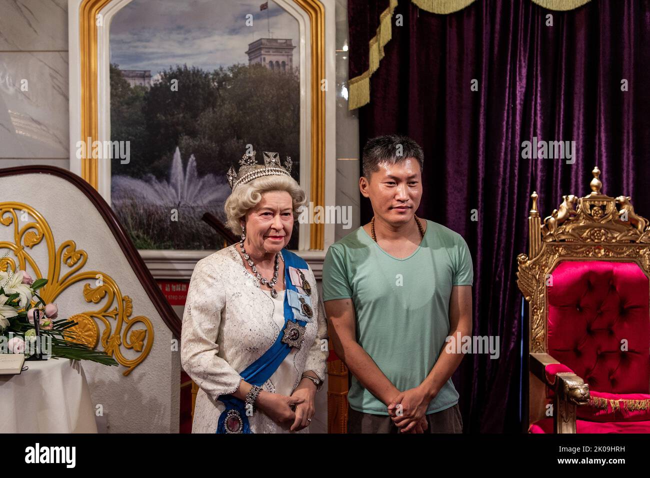 A man poses next to wax sculpture of Queen Elizabeth II at Wuhan Madame ...
