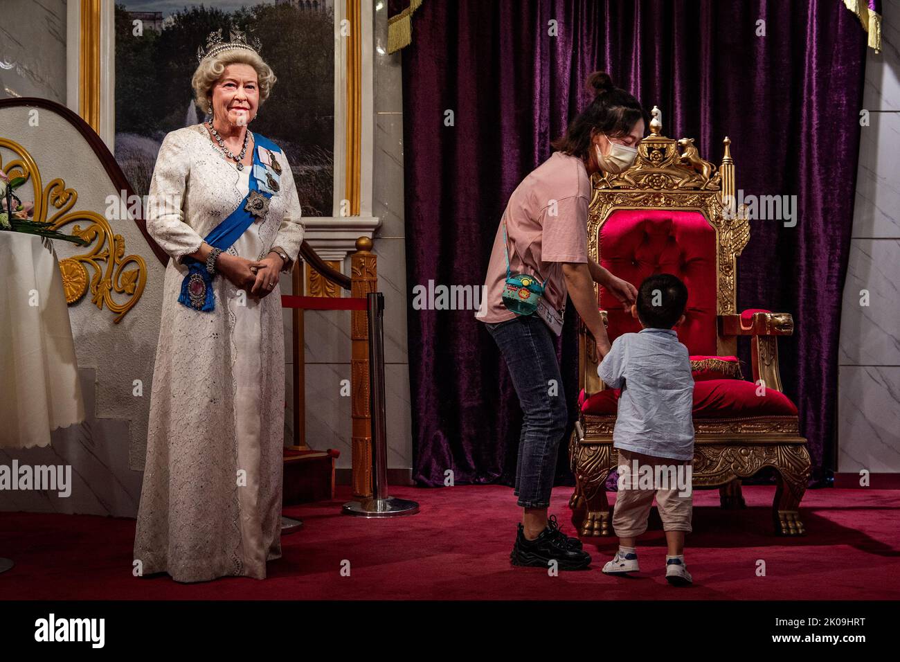 A woman and her kid stand beside a wax sculpture of Queen Elizabeth II ...
