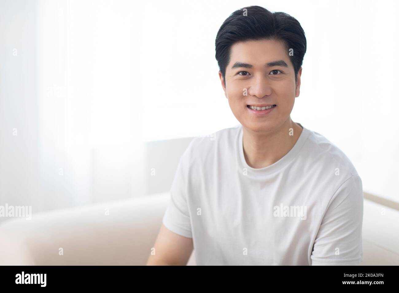 Cheerful young Chinese man sitting on sofa Stock Photo - Alamy