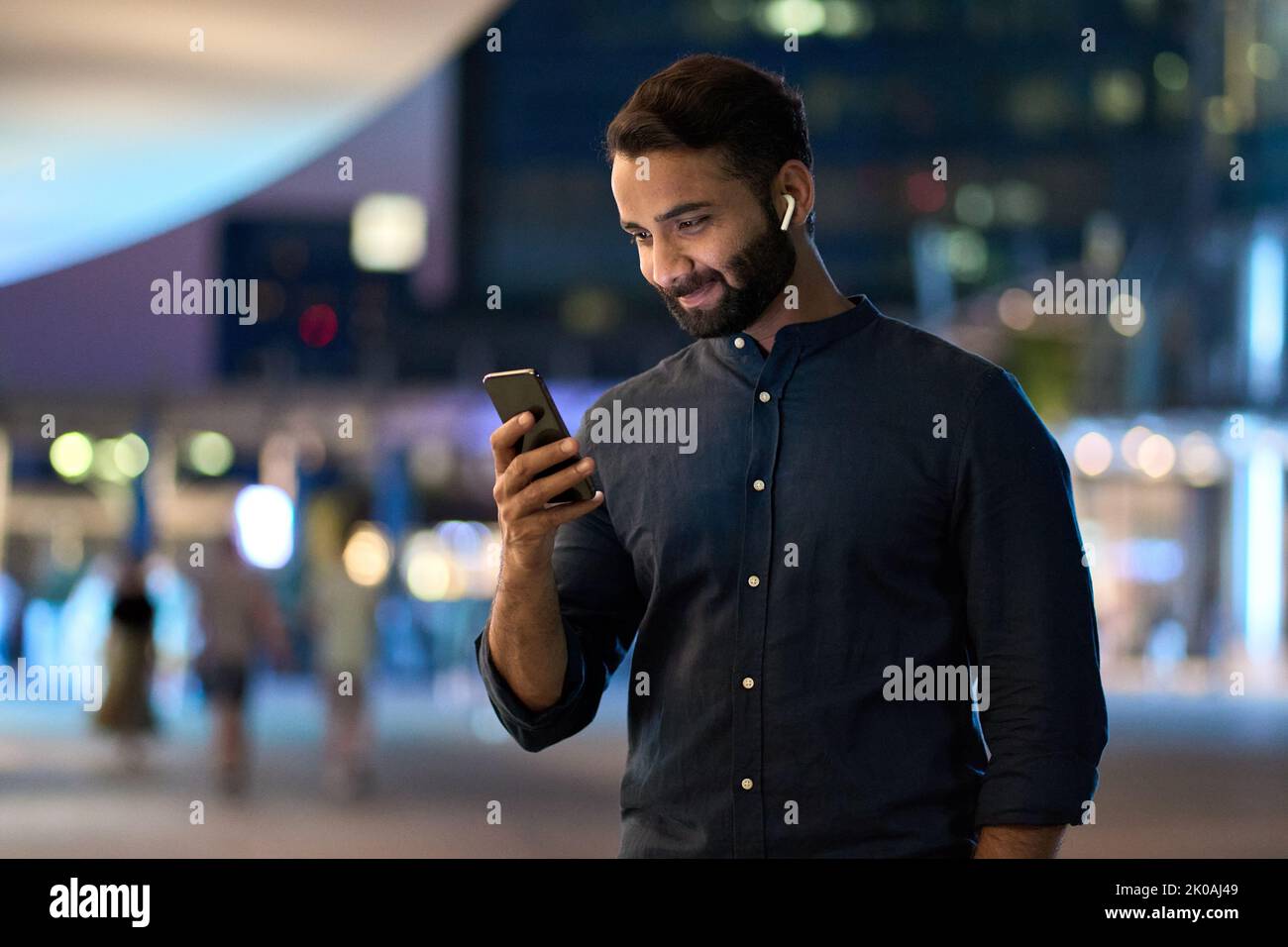 Indian business man wearing earbud standing in night city using ...