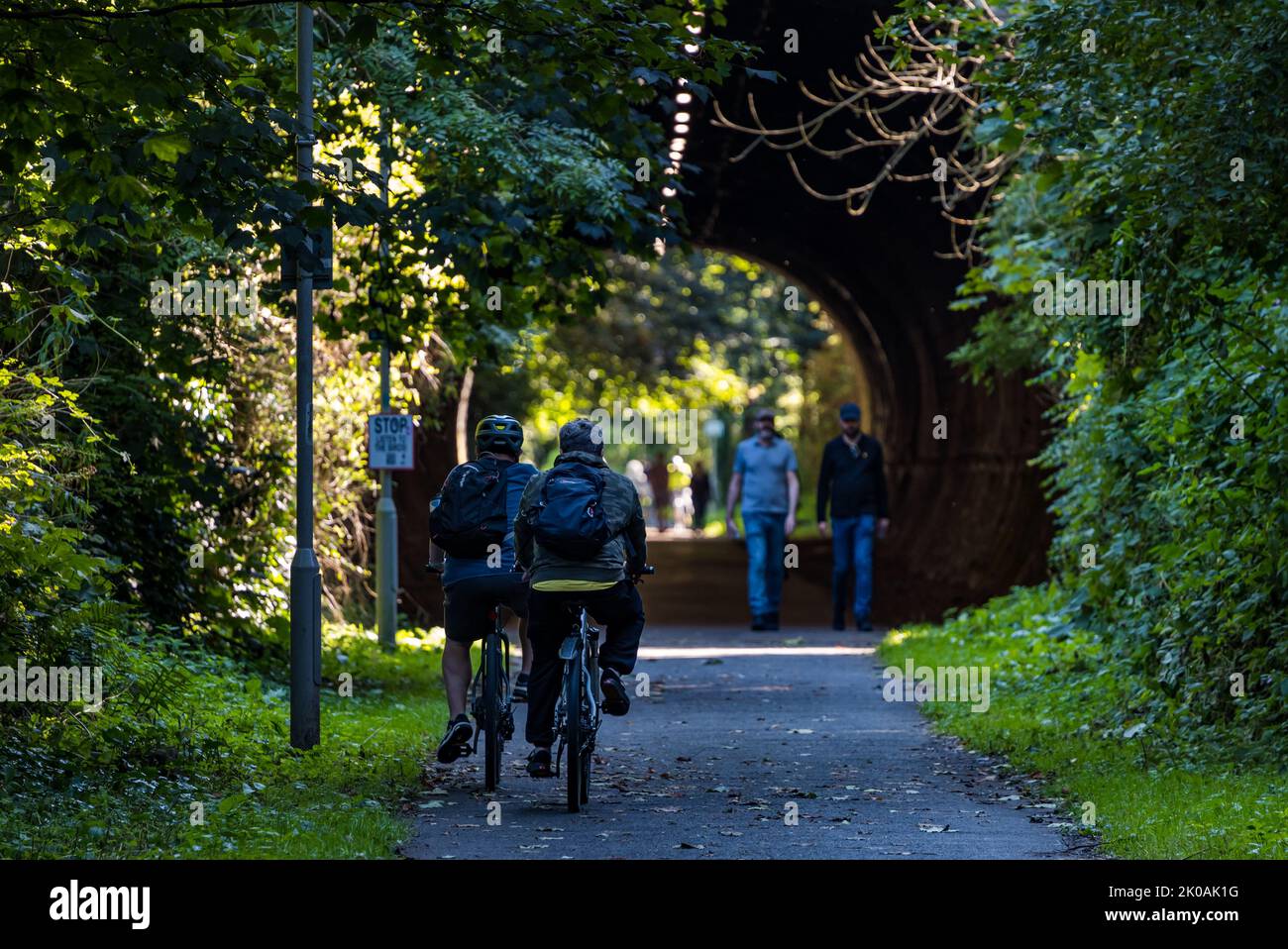 People walking and cyclists riding bikes through tunnel on railway path ...