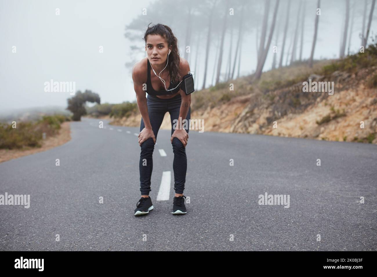 Sporty young woman taking a break from running on a road in the morning ...