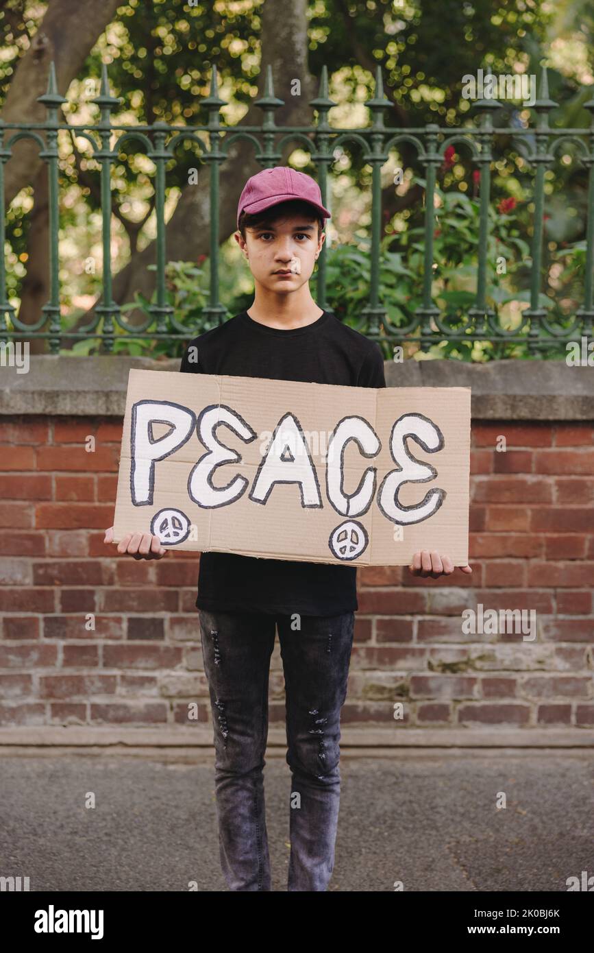 Teenage boy looking at the camera while holding a peace poster. Young ...