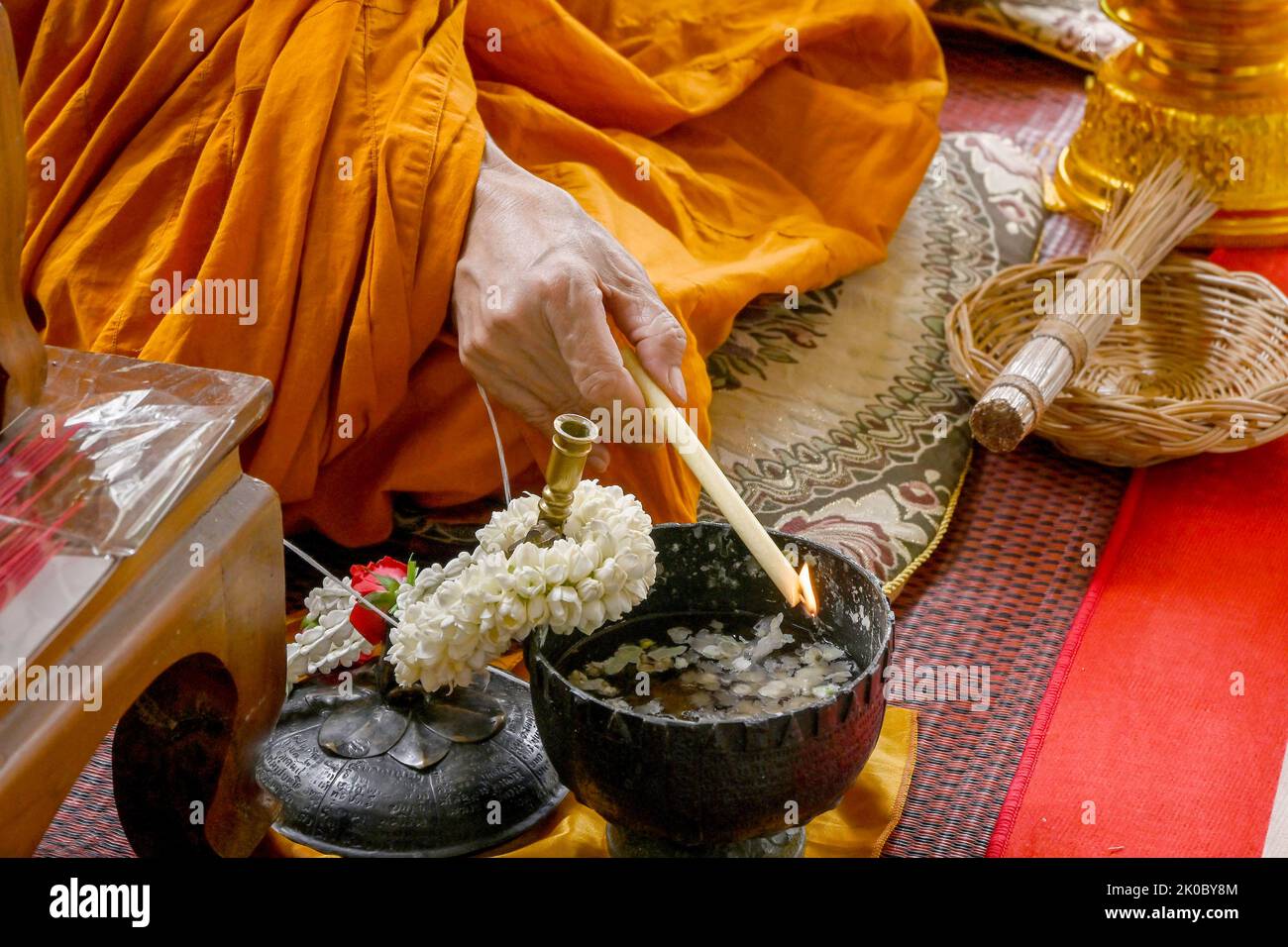 A close up view of a Thai monk dripping wax into a bowl of holy water ...