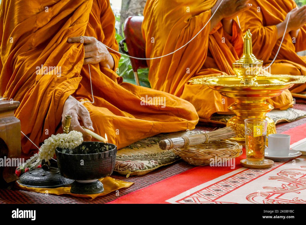 A close up view of a Thai monk dripping wax into a bowl of holy water ...