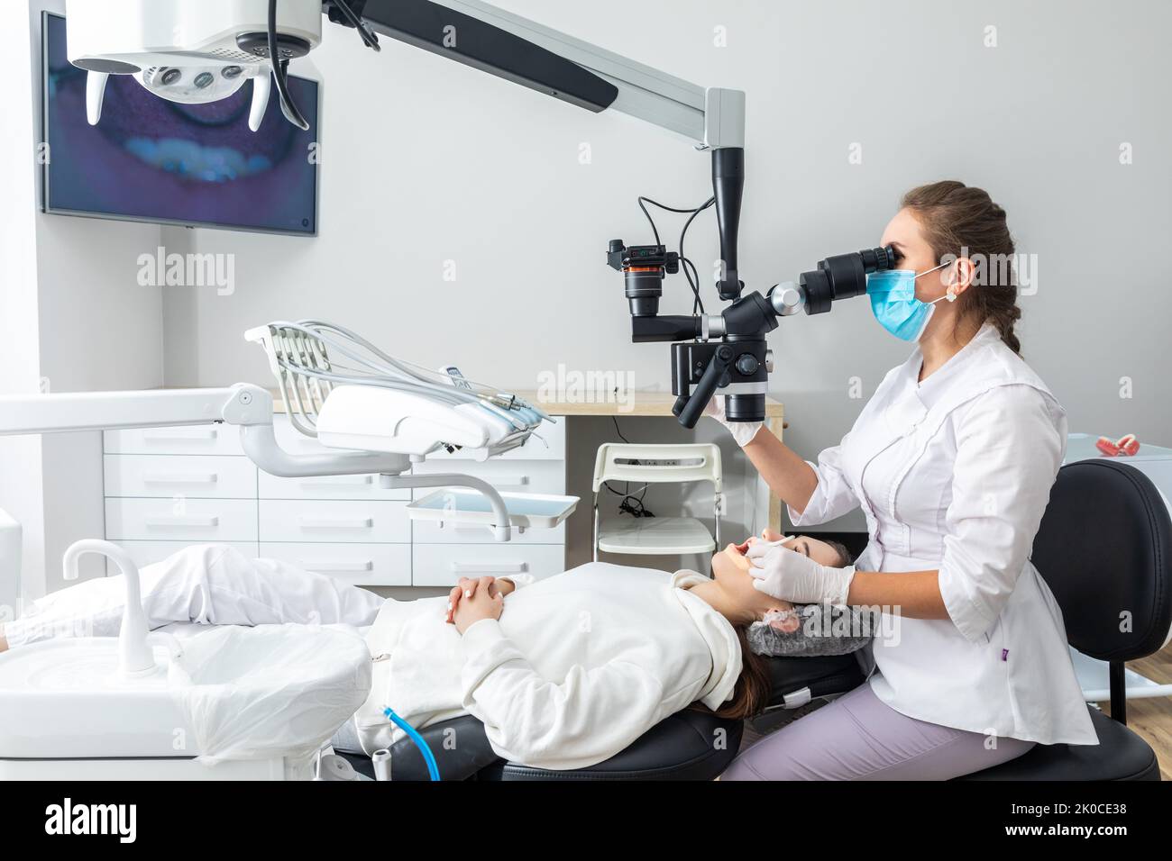Female dentist using dental microscope treating patient teeth at dental ...