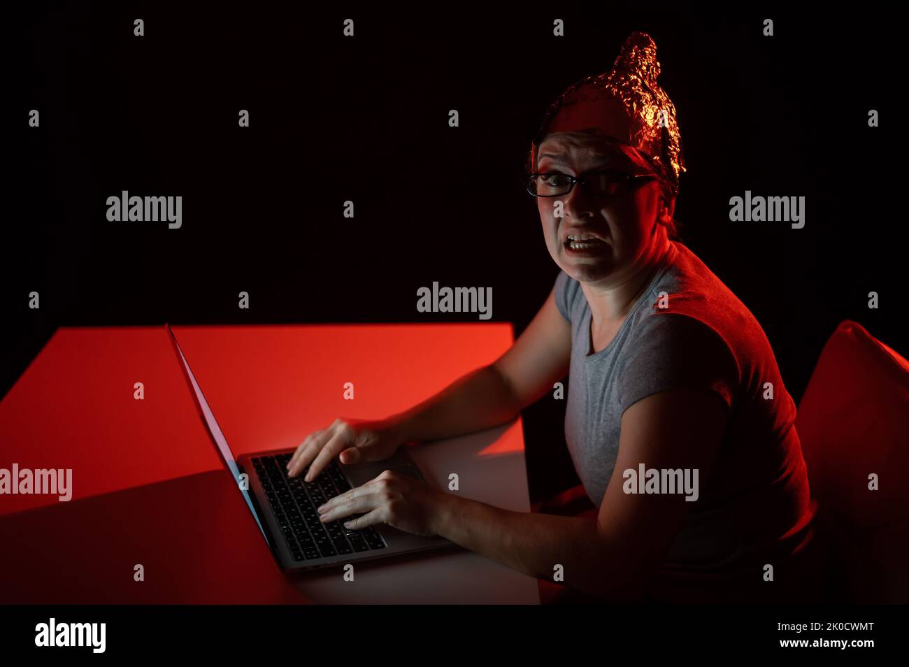 Paranoid caucasian woman typing on a computer wearing a tinfoil cap ...